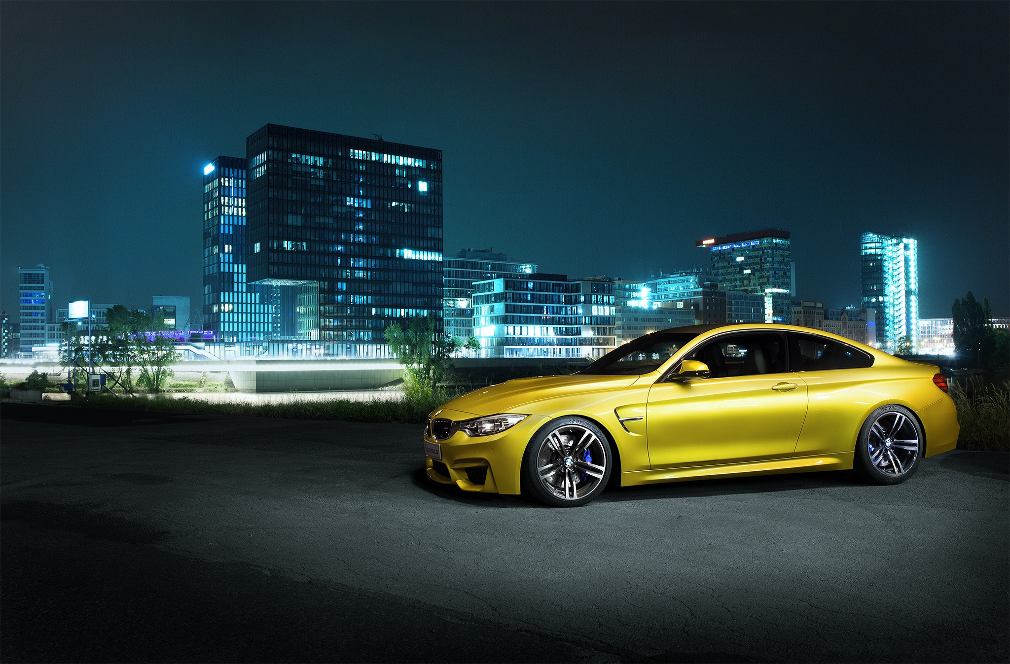 A gold BMW F82 M4 stands against the backdrop of a city at night ...
